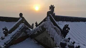 Telhado coberto de neve com elementos arquitetônicos tradicionais, céu claro e o sol se pondo ao fundo.