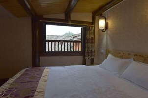Quarto com cama, janela com vista para edifícios e luminária fixada na parede.