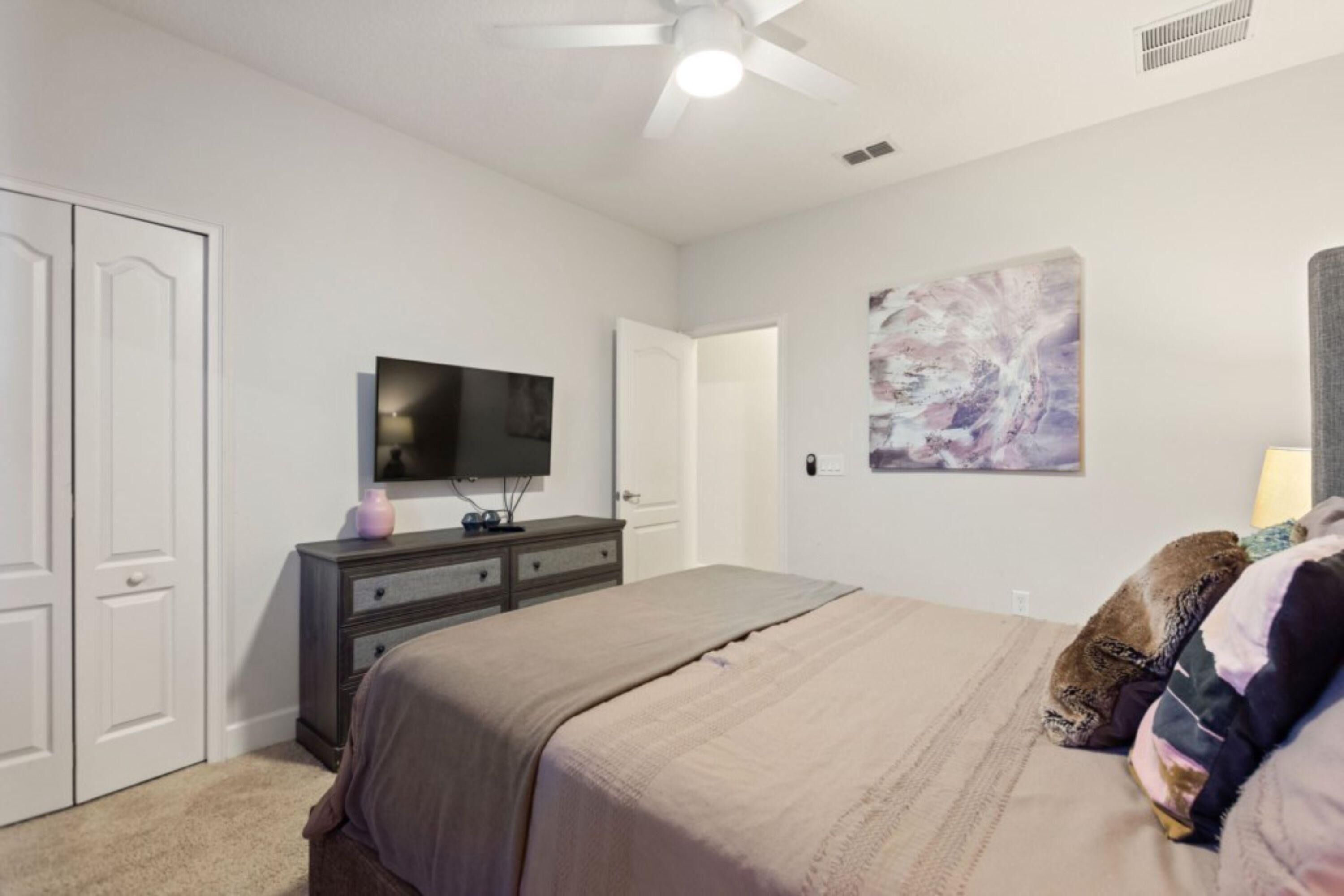 Quarto com cama, penteadeira, televisão e ventilador de teto.