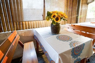 Uma mesa com toalha estampada, um vaso com girassóis e um banco de madeira.