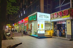 Uma rua com diversas lojas, incluindo uma loja de chá e um estabelecimento com uma placa que diz 'LEMON MIRKY TEA'.