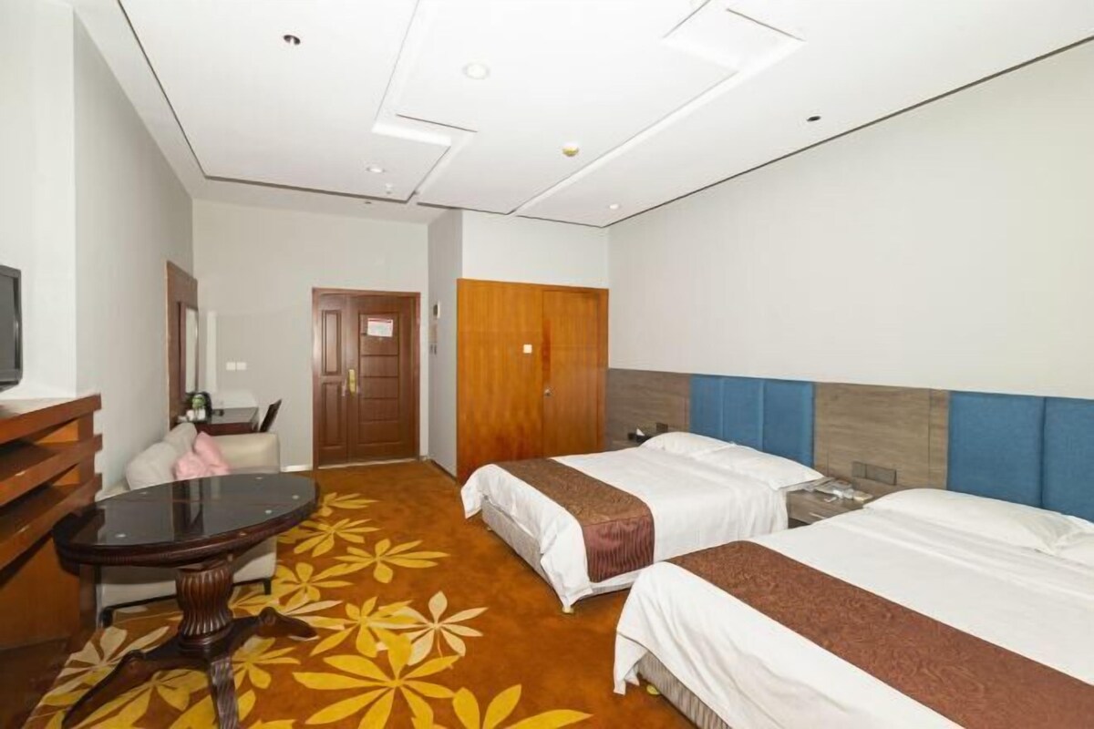 Quarto de hotel com duas camas, uma escrivaninha, uma cadeira, uma televisão e uma porta.