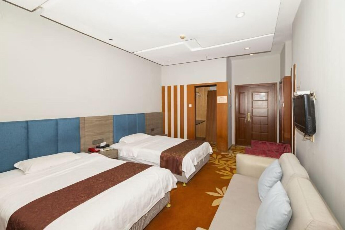 Quarto de hotel com duas camas, um sofá, uma televisão e uma porta que dá para outro espaço.