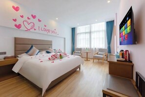 Quarto de hotel moderno com uma cama grande, televisão, escrivaninha e área de estar.