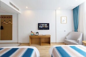 Quarto de hotel com duas camas, uma escrivaninha, uma cadeira, televisão e um cabideiro.