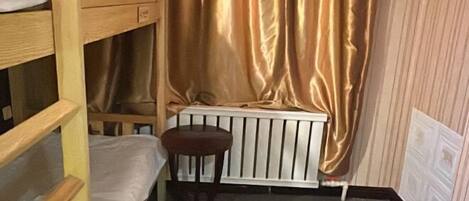 Quarto com beliche, um radiador, um banquinho e uma cortina.