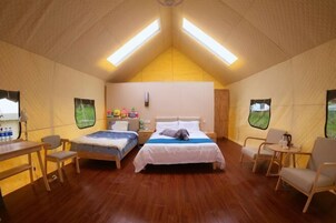 Um quarto tipo tenda com duas camas, uma escrivaninha, cadeiras e uma pequena mesa.