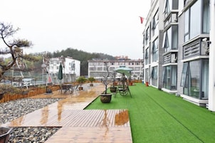 Jardim no terraço com deck de madeira, grama sintética verde e plantas em vasos.