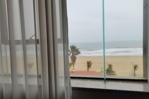 Vista da praia através de uma janela com persianas entreabertas.