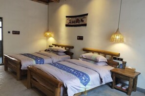 Quarto com duas camas de madeira, uma mesinha de cabeceira pequena de madeira, uma tapeçaria na parede e duas luminárias pendentes.