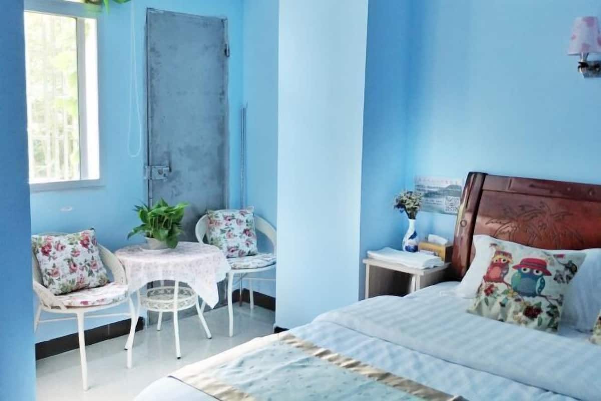 Quarto com uma cama, uma mesinha com uma planta, duas cadeiras e uma janela.
