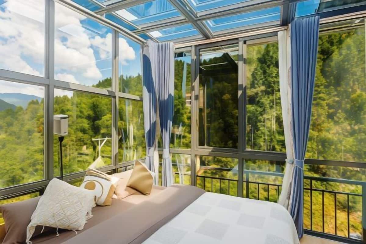 Quarto com uma grande janela, uma cama e vista para uma floresta.