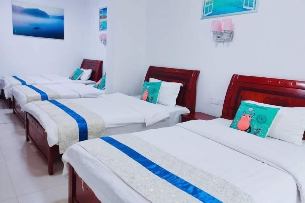 Quarto de hotel com três camas, cada uma com cabeceira de madeira e roupa de cama branca.