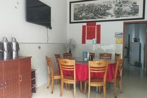 Uma sala de jantar com mesa, cadeiras, televisão e geladeira.