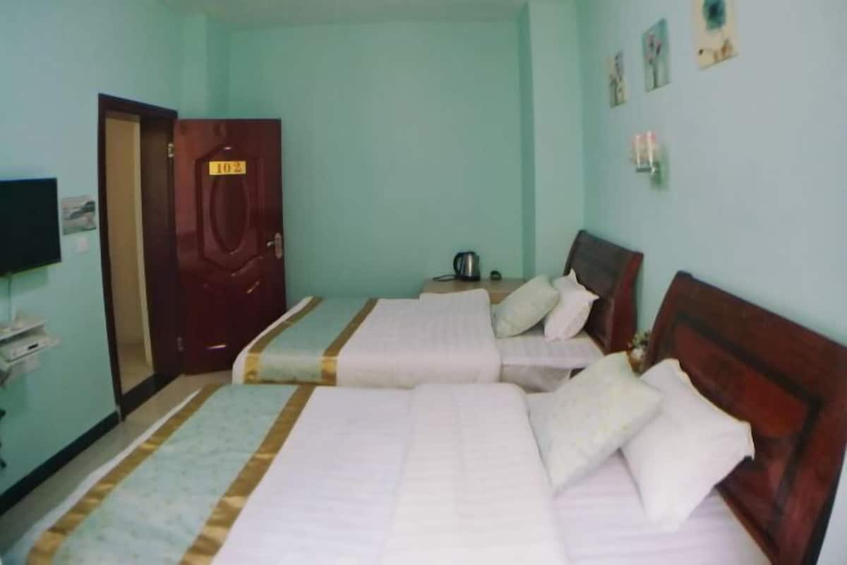 Quarto com duas camas, televisão, porta com um número e uma pequena mesa com chaleira.