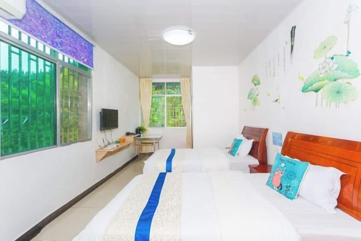 Quarto de hotel com duas camas, televisão, escrivaninha e janela com vista para áreas verdes.