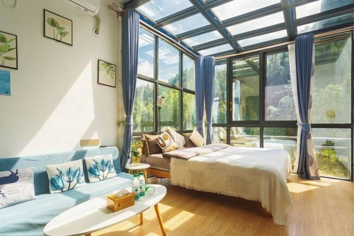 Quarto com cama, sofá, uma mesa pequena e uma janela grande com cortinas.