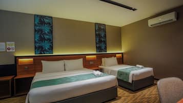 Quarto de hotel com duas camas, uma escrivaninha e uma cadeira. Há um aparelho de ar condicionado na parede e uma obra de arte na parede acima das camas.