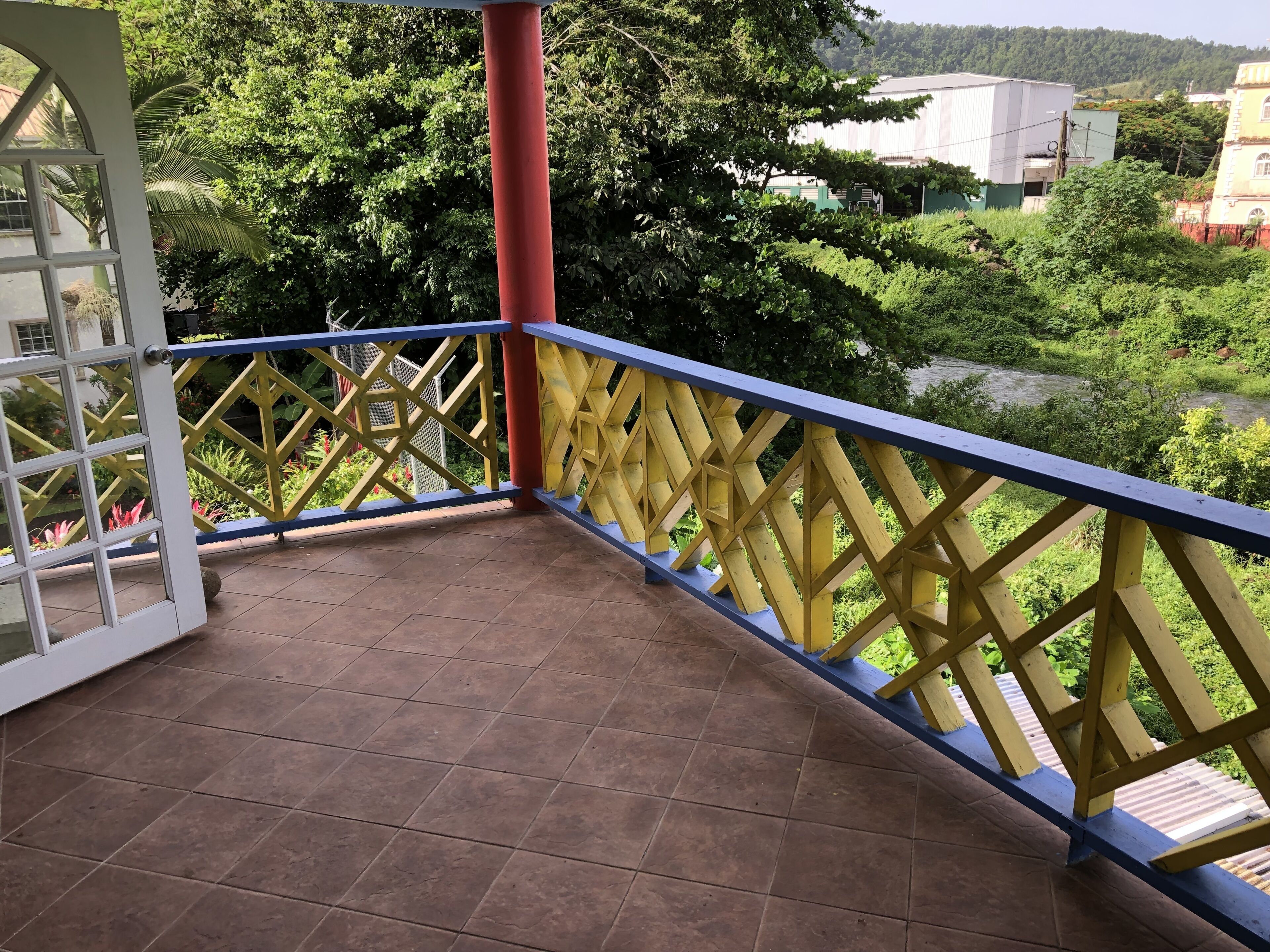 Uma varanda com chão de azulejos, grades de madeira amarela e um pilar vermelho.