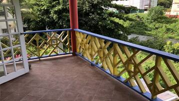 Uma varanda com chão de azulejos, grades de madeira amarela e um pilar vermelho.
