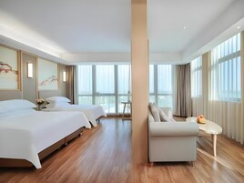 Quarto de hotel com duas camas, área de estar e amplas janelas.