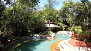 Uma área de piscina rodeada por árvores, com um deque de madeira e um gazebo.