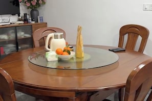 Uma mesa de vidro redonda com um jarro branco, uma tigela de laranjas e um saco de papel.