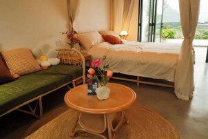 Quarto com cama, sofá, mesa de madeira redonda e janela com cortinas.