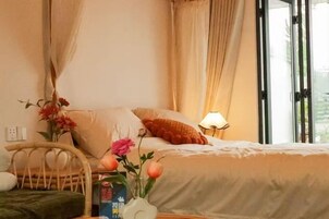 Quarto de hotel com cama, uma cadeira, mesa de cabeceira com abajur e janela com cortinas.