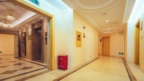 Corredor de hotel com piso de mármore, uma lixeira vermelha e um elevador.