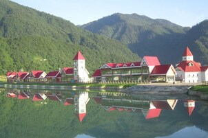 Hotel na beira do lago com vários edifícios de telhado vermelho, uma torre central e reflexo na água.