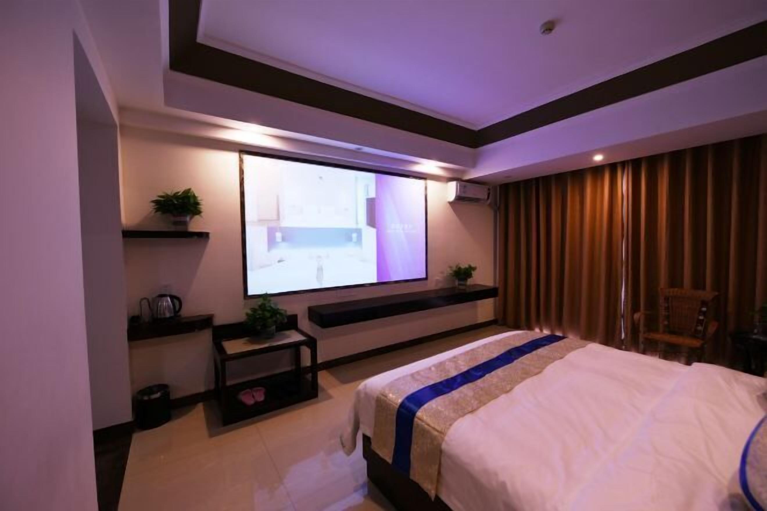 Quarto de hotel moderno com uma cama grande, televisão de tela plana na parede, uma mesinha com uma planta e uma cadeira.
