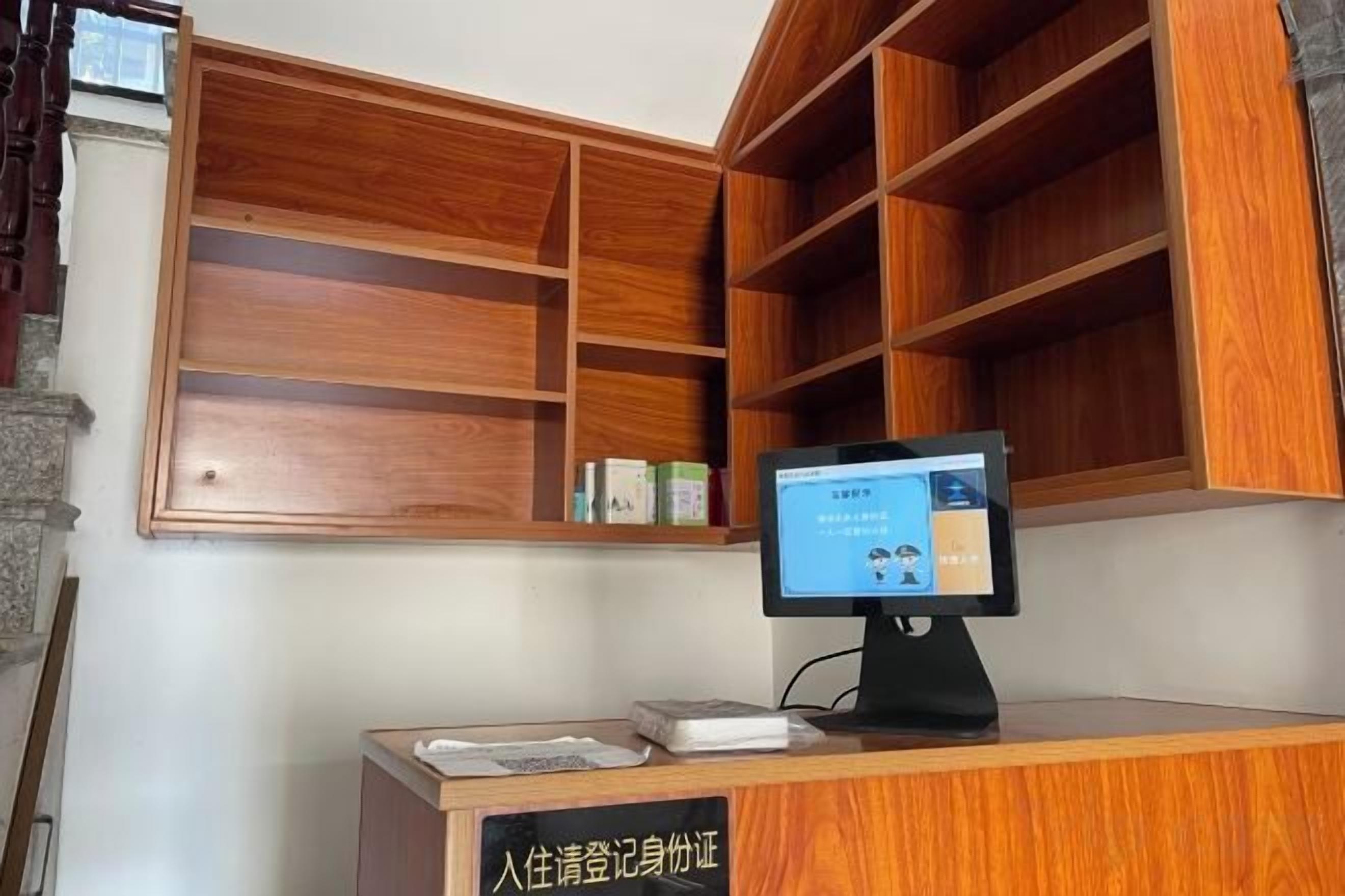 Bancada de recepção com monitor de computador, prateleiras de madeira e placa indicando área de registro.