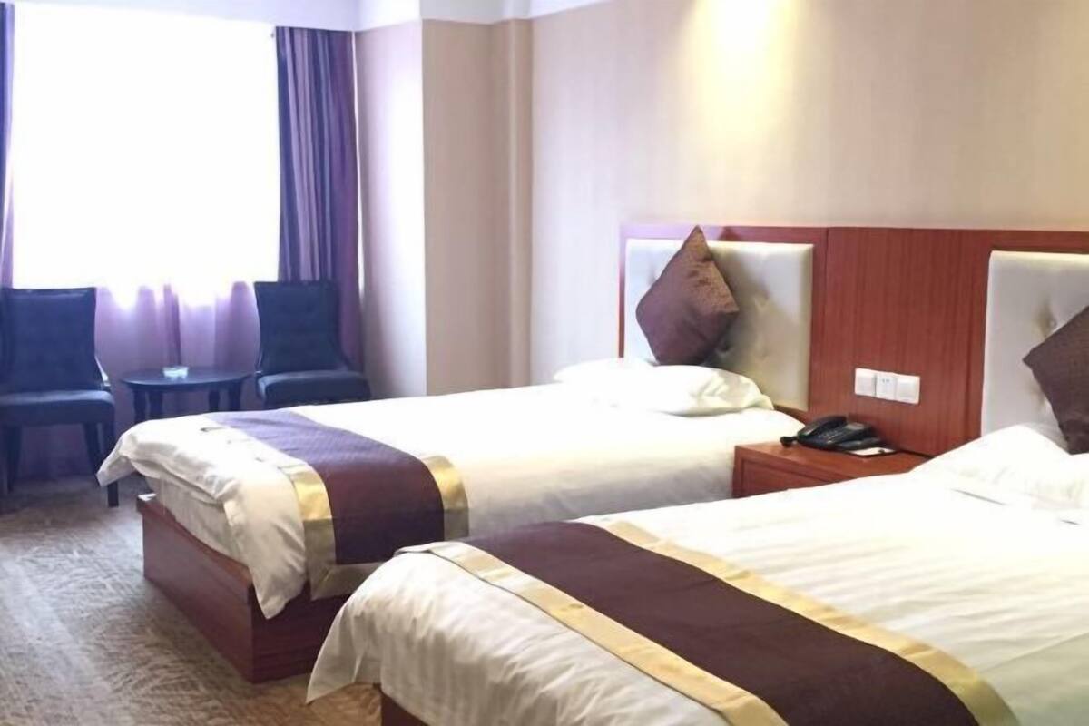 Quarto de hotel com duas camas, uma escrivaninha, uma cadeira e uma janela com cortinas.
