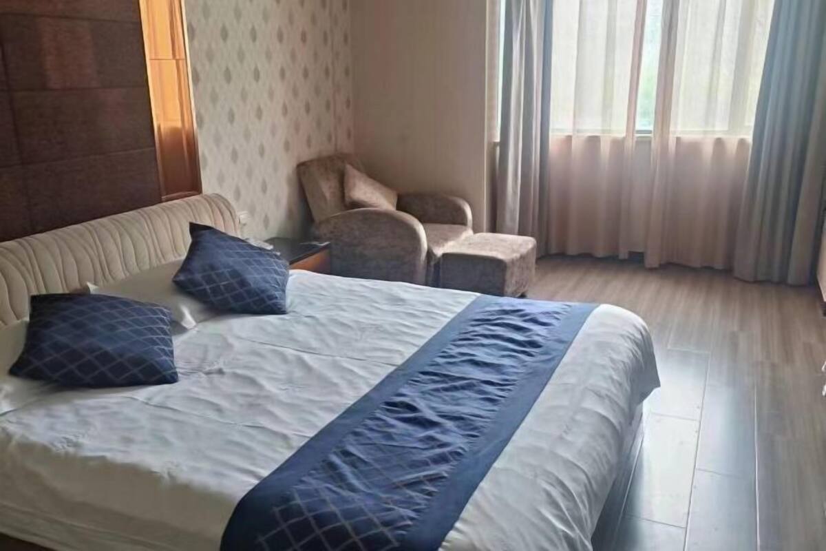 Quarto de hotel com cama, uma cadeira, janela com cortinas e papel de parede estampado.