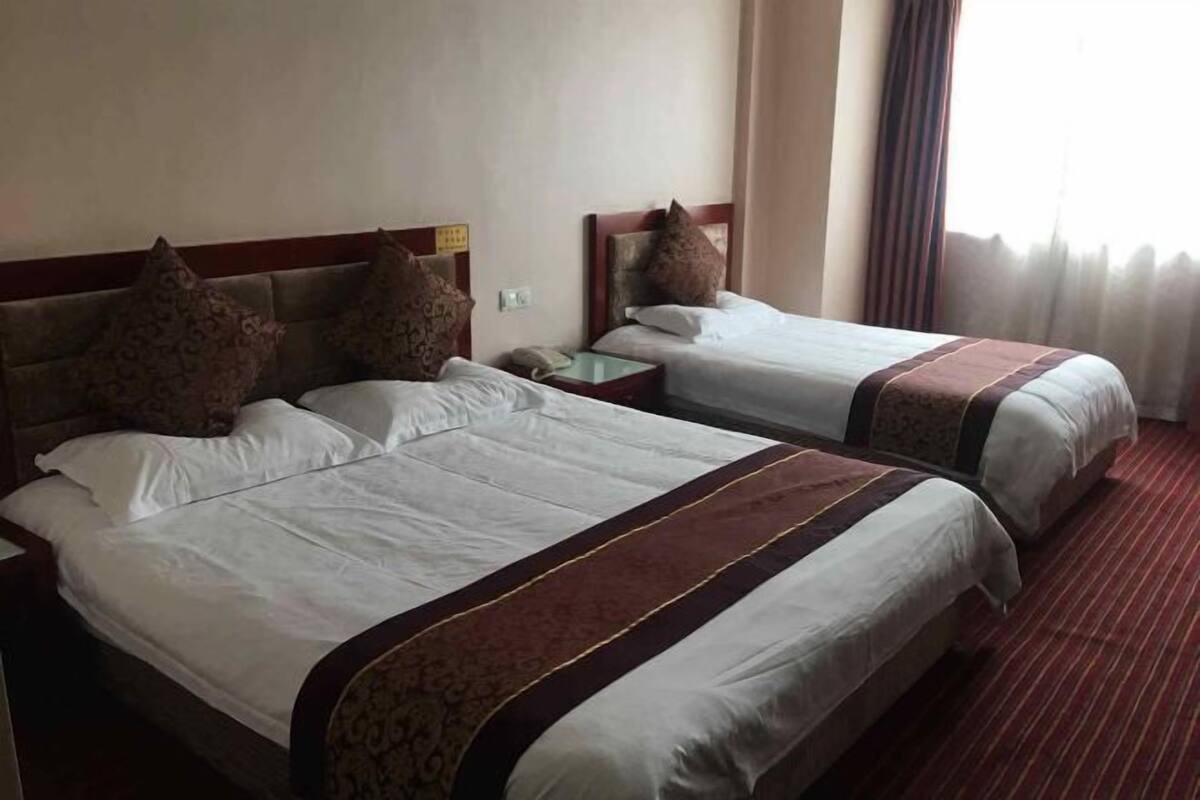 Quarto de hotel com duas camas, uma mesinha de cabeceira, um telefone e uma janela com cortinas.