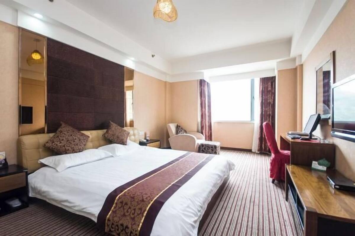 Quarto de hotel com uma cama grande, uma escrivaninha, uma cadeira, uma televisão e uma janela.