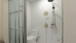 Casa de banho com chuveiro em cabine de vidro, sanita e lavatório fixado na parede.