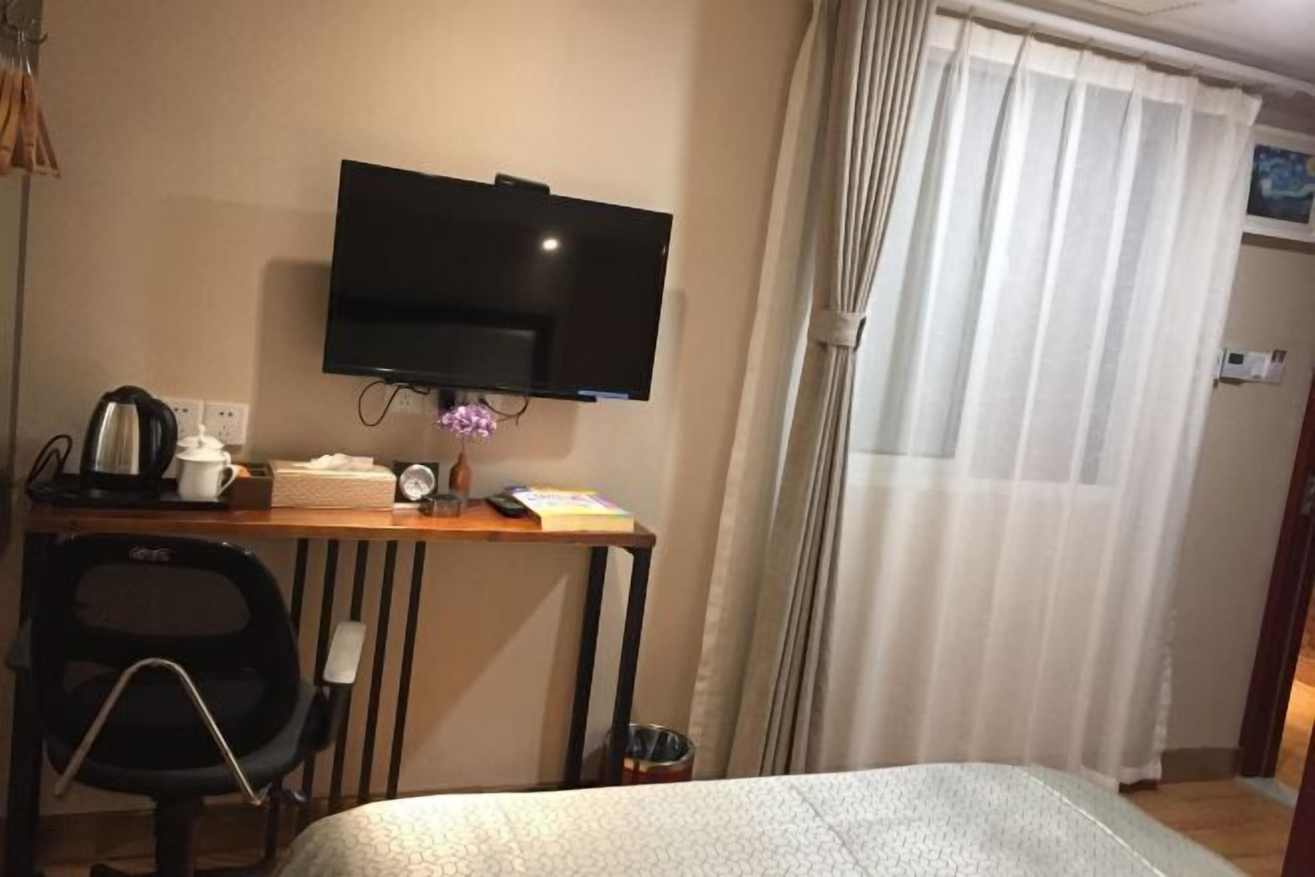 Quarto de hotel com cama, escrivaninha com televisão, cadeira, cafeteira e pequena mesa com um vaso de flores.
