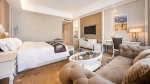 Quarto de hotel com cama, sofá, televisão, escrivaninha e luminária.