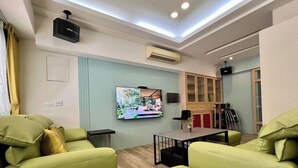 Uma sala de estar moderna com sofás verdes, uma TV de tela plana, um aparelho de ar condicionado e um armário de madeira.