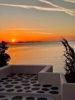 Terraço com vista para o pôr do sol sobre o mar, com guarda-corrimão branco e piso estampado.