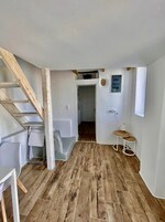 Quarto com escada de madeira, uma mesa pequena e uma porta que dá para outro aposento.