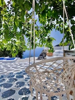 Uma cadeira de vime com vista para um chão azul e branco, uma rocha e um vaso com planta.