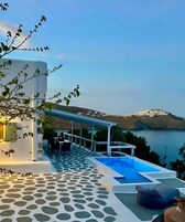 Uma área moderna com piscina ao ar livre, vista para uma ilha distante e para o mar.