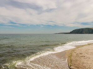 Uma praia com ondas, um areal e um penhasco ao longe.