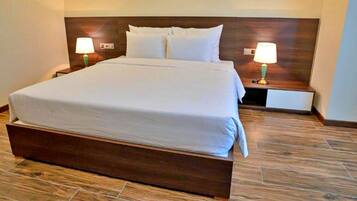 Uma cama grande com cabeceira de madeira, duas mesas de cabeceira com luminárias e piso de madeira.