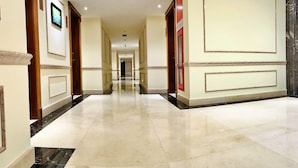 Corredor de hotel com piso de mármore, portas de madeira e obras de arte emolduradas nas paredes.