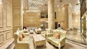 Um hall de entrada luxuoso, com sofás ornamentados, um balcão de recepção de mármore e um candelabro.