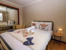 Quarto de hotel com uma cama, uma cadeira, mesa de cabeceira com abajur e um espelho.